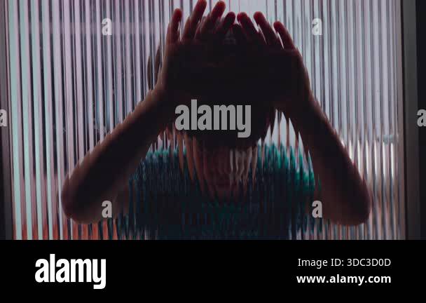 Child stands behind textured glass with both hands against the surface ...