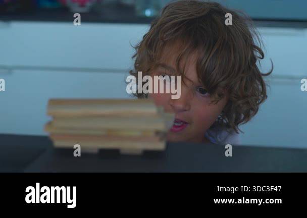 A boy adds a block to a low wooden arrangement with quiet focus ...