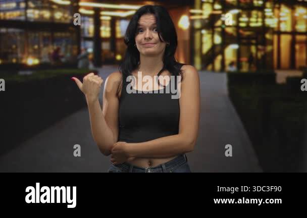 Woman in black tank top and denim jeans points thumb over shoulder to ...
