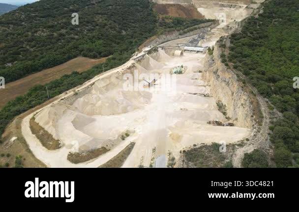 Open-pit quarry with heavy machinery transporting stone in a hillside ...