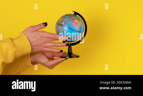 Female hands spinning a small globe on a bright yellow background ...