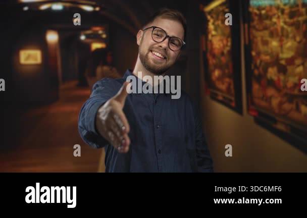 Man wearing glasses smiles and extends hand for handshake in gallery ...