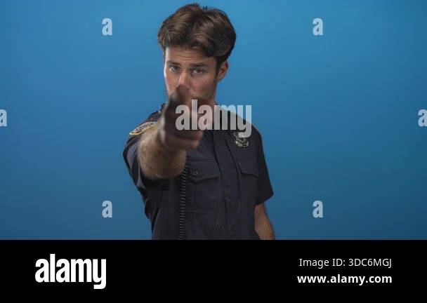 Policeman man pointing finger toward camera in blue studio wearing navy ...
