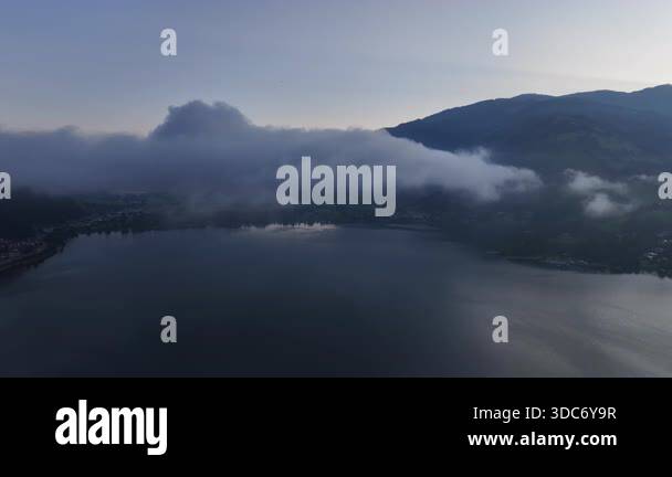 Aerial fog bank over mountain lake at dawn, low cloud hugging shoreline ...