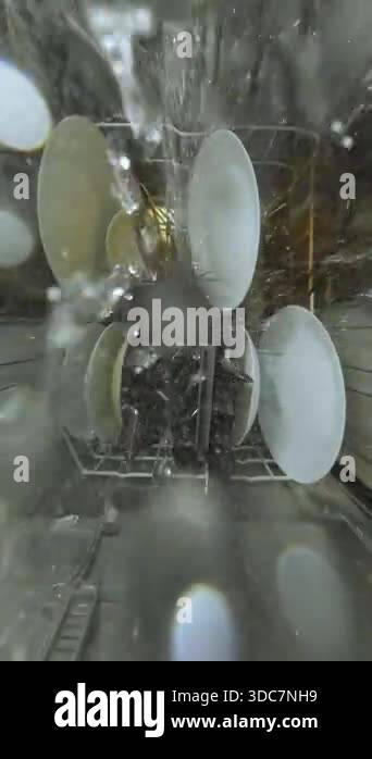 Inside view of a running dishwasher with water spraying over dishes and ...