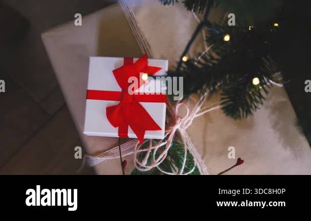 Wrapped holiday gift box with red ribbon near decorated Christmas tree ...
