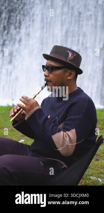 A musician plays his instrument on a sabo dam surrounded by grass. A ...