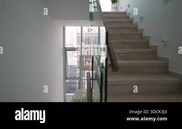 Modern staircase with glass handrail, stone steps rising toward bright ...