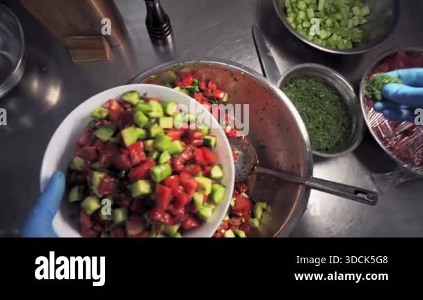 A manwearing blue gloves stands in the kitchen at the cutting table and ...