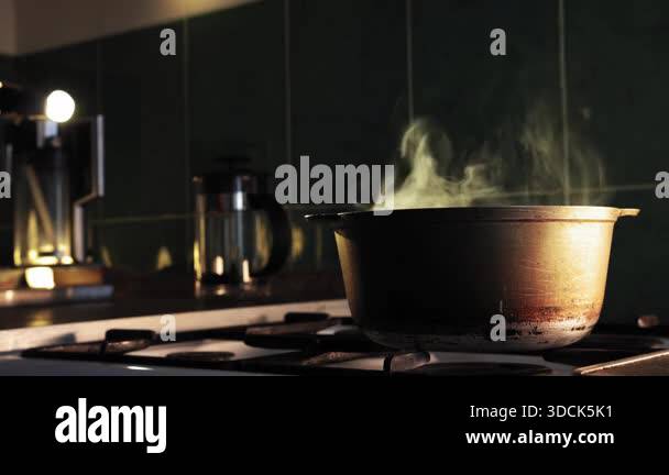In a dark kitchen, a man slowly pours pasta from his hand into a pot of ...