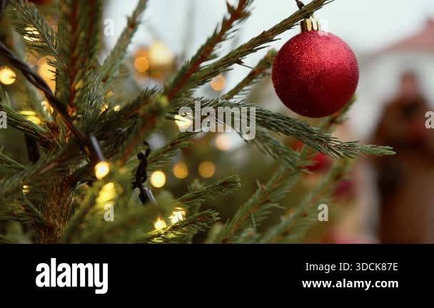 Red glitter bauble hangs on evergreen branch decorated with warm ...