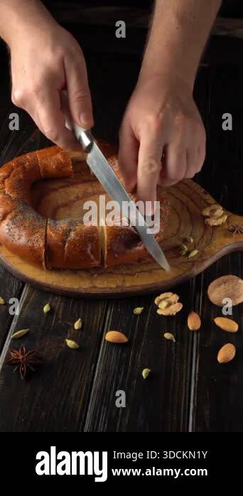 Hands are seen slicing a round pastry on a wooden board. Nuts and ...