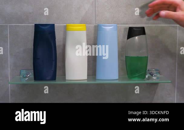 Shampoo on glass shelf in bathroom. Taking shower gel jar in hand to ...