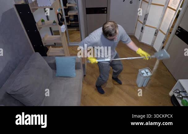 A cleaner dancer in an apartment. A man washes the floor with a mop ...