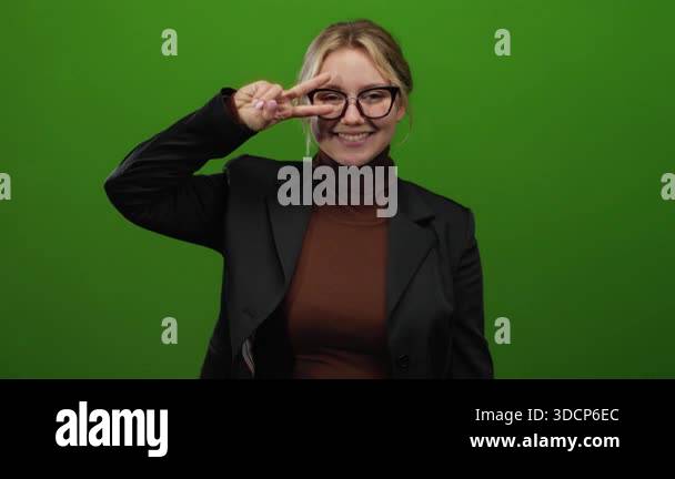 Woman smiling and posing with peace sign in front of green background ...