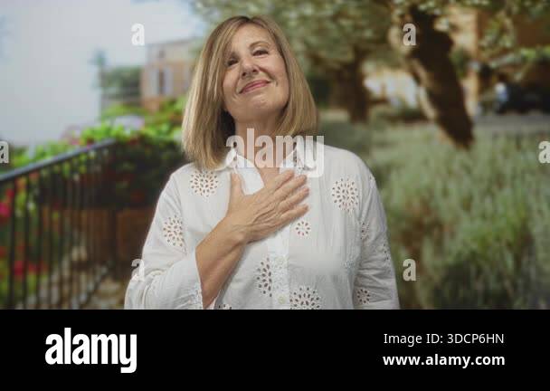 Woman clutching her chest and smiling softly while standing near ...