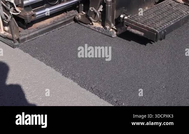 Heavy machinery lays down asphalt on new roadway construction process ...