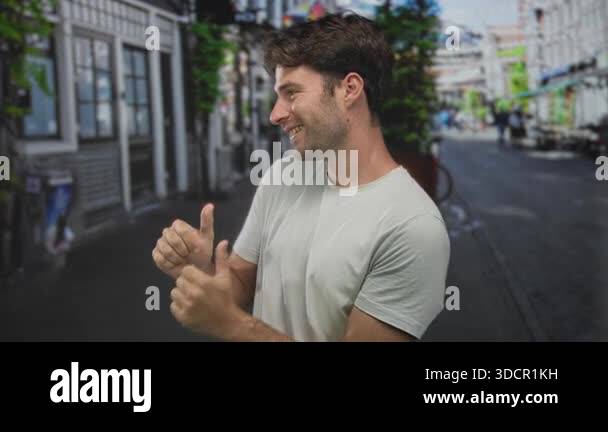 Man giving thumbs up on a city street while smiling and glancing ...