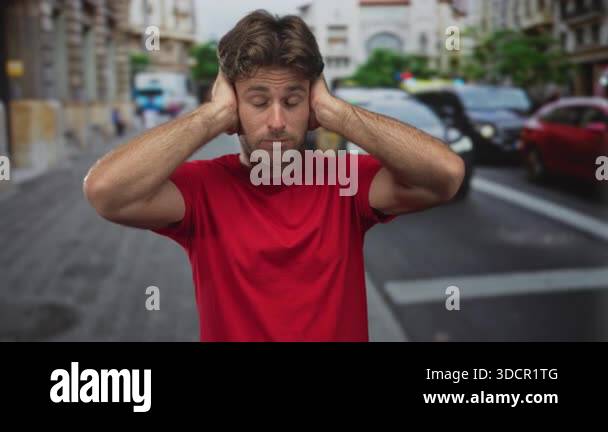 Young hispanic man in red t shirt covering ears with hands amid busy ...