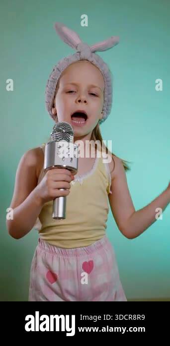 Vertical. Young child with bunny ears headband singing into a sparkling ...