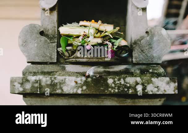Canang Sari offering placed on a traditional Balinese stone shrine with ...
