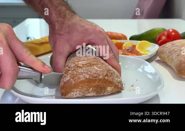 A hand cuts a loaf of bread on a wooden cutting board in a kitchen ...