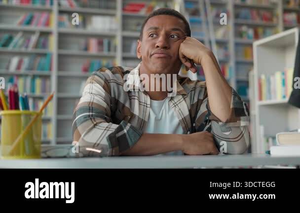 Pensive thoughtful African American man male student in library leaning ...