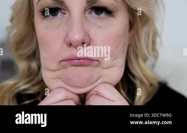 mature woman touches her chin and neck area assessing excess fat under ...