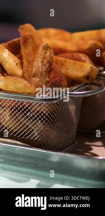 Warm lighting highlights hand reaching for fries in metal basket ...