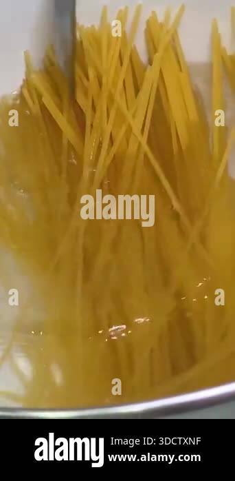 Hands gently lower a tied bundle of spaghetti into a pot of boiling ...