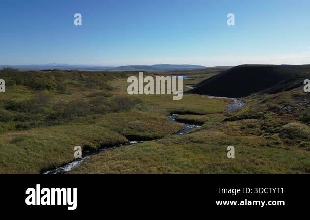Iceland aerial view. A river runs through a grassy field with a clear ...