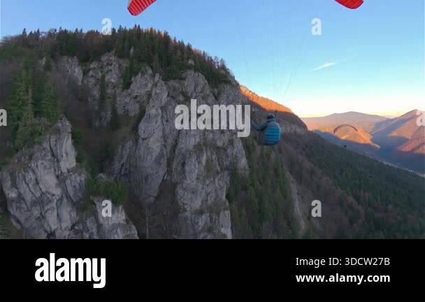 Paragliders glide calmly past a rocky cliff in autumn mountains ...