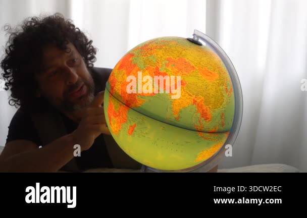 Man at home look at a globe and rotate it, choosing a random country to ...