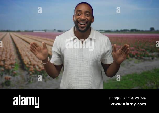 Man clapping hands and smiling while standing among long rows of tulips ...