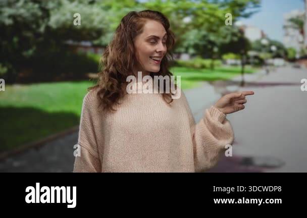 Woman smiling in a park pointing while gesturing a phone call symbol ...