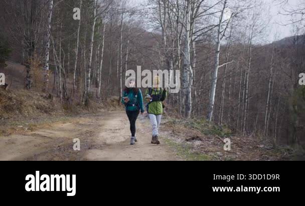 Two female friends hike on a dirt road, enjoying the mountain scenery ...