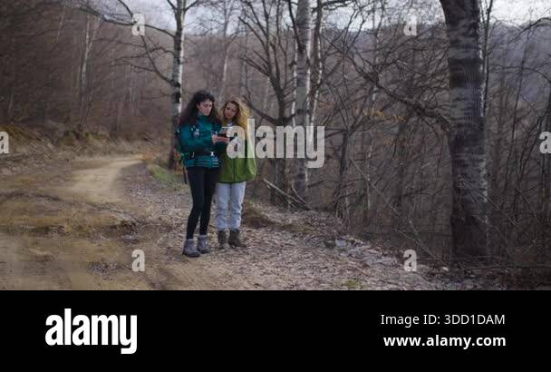 Two female friends hiking on a dirt road in the mountains, consulting a ...