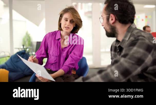Two team members share ideas while reviewing plans in an office. The ...