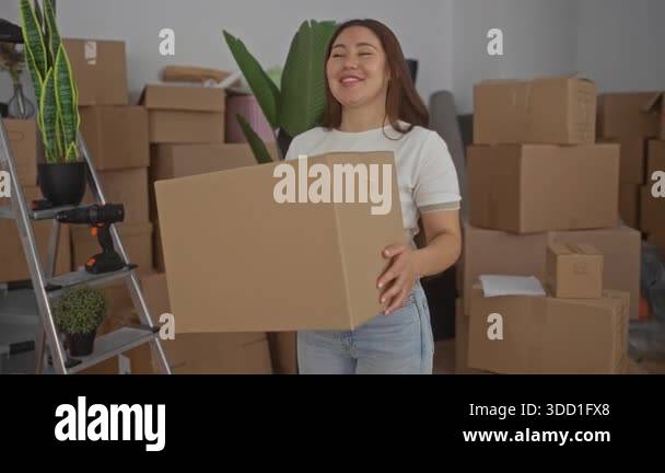 Smiling woman wearing a white t shirt and jeans carrying a cardboard ...