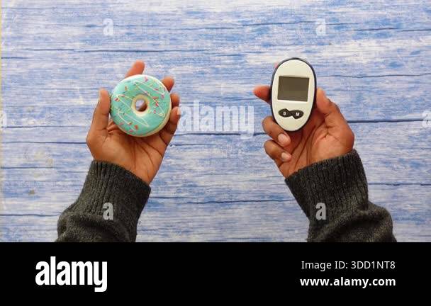 A person holds a donut in one hand and a blood sugar monitor in the ...