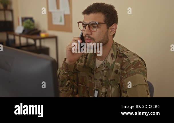 Young hispanic man in camouflage uniform holds phone to ear at desk ...