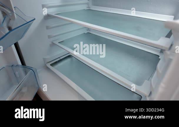 An empty refrigerator shows clear shelves and no food items inside ...