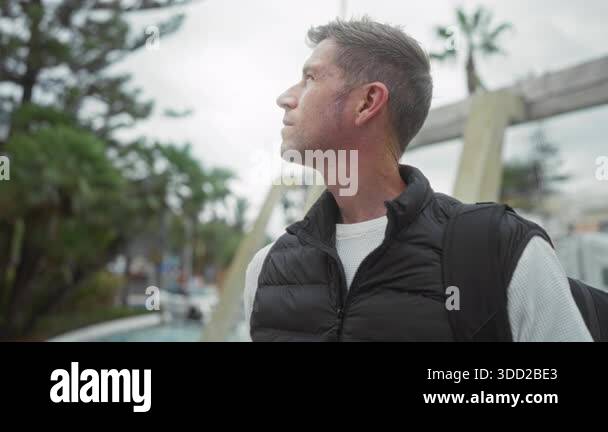 Young man standing on a city street, wearing a black vest, looking ...