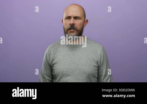 Bearded bald man in a gray sweater gestures pointing forward against a ...