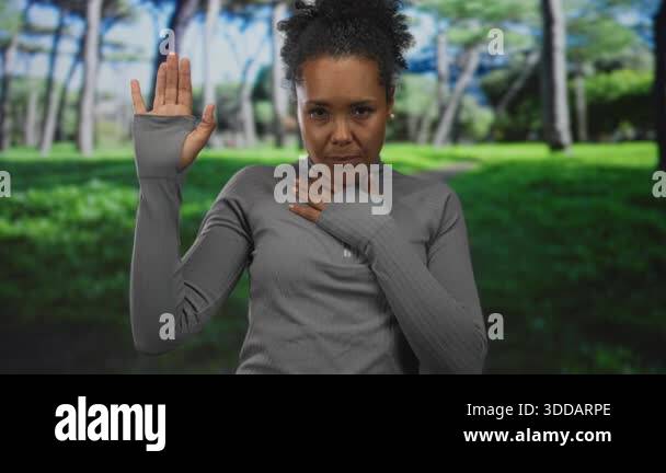 Woman stands amid green trees in a forest raising her hand in greeting ...
