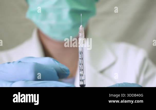 A doctor removes air bubbles from the syringe after filling it with ...