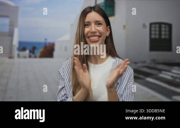Young hispanic woman claps hands on sunlit street in front of white ...