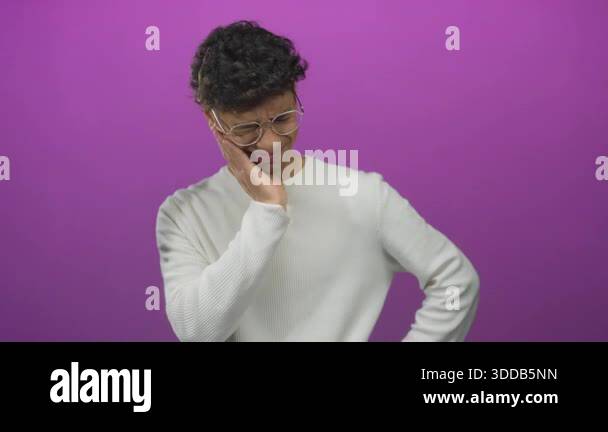 Man gently rubbing cheek in vivid purple studio set with glasses and ...