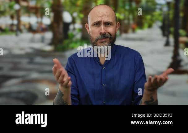 Bearded man standing outdoors on a blurred city street with trees in ...