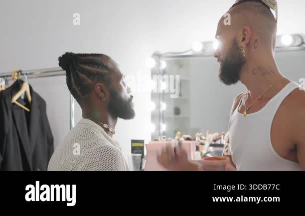 Makeup artist applying foundation to gay man face in dressing room with ...